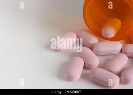 pink tablet pills spilt from a medicine bottle on a white background ...