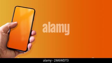 Hand holding a smartphone with blank orange screen. White office ...