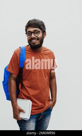 Indian student with blue backpack, glasses and notebook posing on gray ...