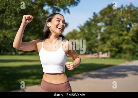 Happy fitness girl achieve goal, finish marathon, running with hands up ...