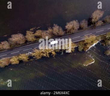 A van drives on. road surrounded by floodwater as the Welney wash fills ...