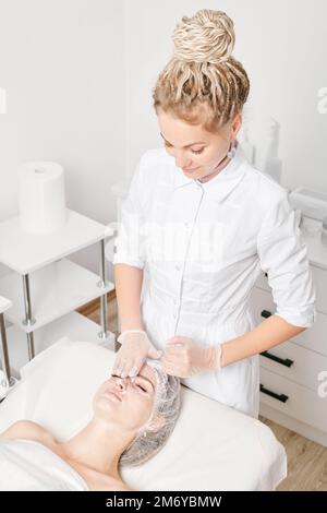 A cosmetologist in a medical mask massages a client in a beauty salon ...