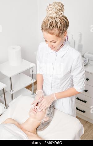 Cosmetologist massages cream mask into woman face skin for rejuvenation ...