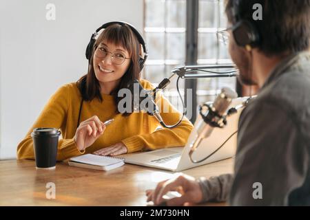 A smiling woman and man podcasting together in a bright studio equipped ...