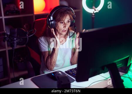 Middle age woman streamer playing video game using computer at gaming ...