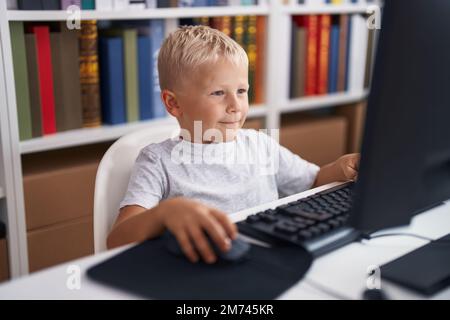 Adorable toddler student using computer sitting on table at classroom ...