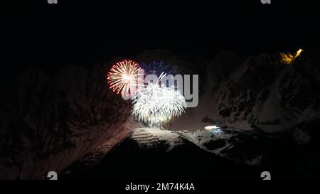 An aerial shot of colorful fireworks on the summit of a snow-covered ...