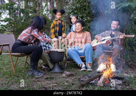 Group of family camper van sitting by fire grilling sausages and ...