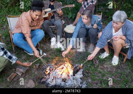 Group of family camper van sitting by fire grilling sausages and ...