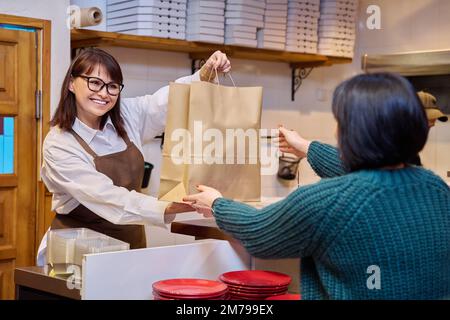 Woman restaurant worker issuing an order for takeaway food in paper bag ...