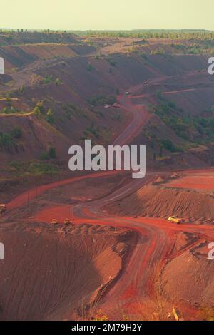Bulldozers and trucks in quarry with red ground. Mining iron ore in ...