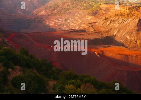 Bulldozers and trucks in quarry with red ground. Mining iron ore in ...