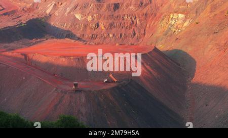 Bulldozers and trucks in quarry with red ground. Mining iron ore in ...