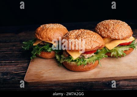 three homemade hamburgers with meat, cheese, lettuce and tomatoes on a ...
