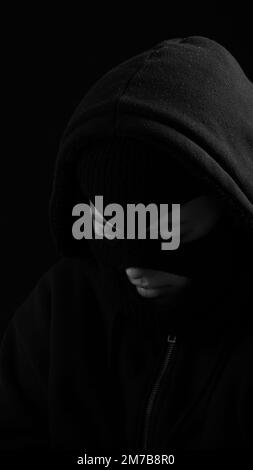 Masked female burglar in black gloves looks over a fence. Crime concept ...