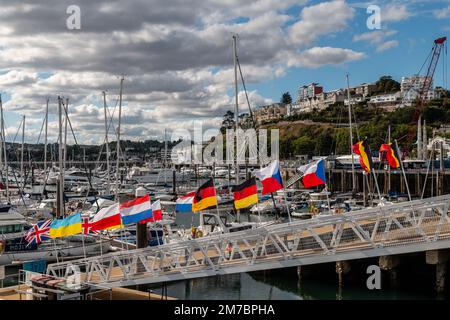 A view across Torquay Harbour showing flags from many countries. In the ...