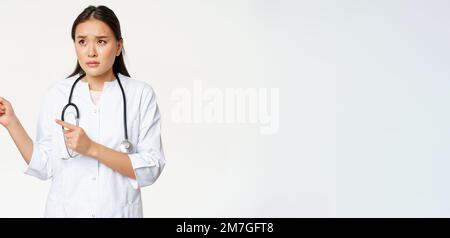 Skeptical female doctor, concerned nurse pointing and looking left with ...