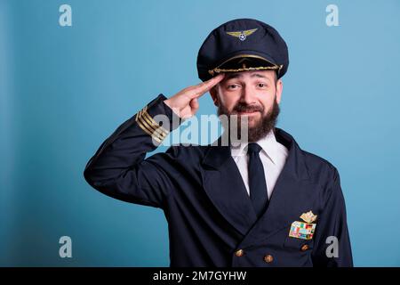 Confident airplane aviator saluting, wearing uniform and hat front view ...