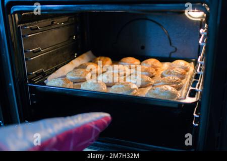 Human hand with an oven glove taking out of the oven a tray with pastry ...