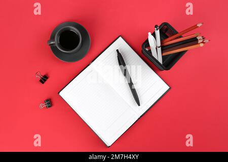 Notebook, stationery holder, paperclips and cup on red background Stock ...