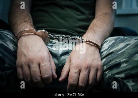 military soldier in handcuffs, hands behind his back, on a dark ...