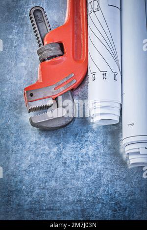 Pipe wrench rolled up engineering drawings on metallic background ...