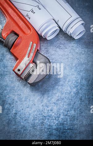 Pipe wrench rolled up engineering drawings on metallic background ...