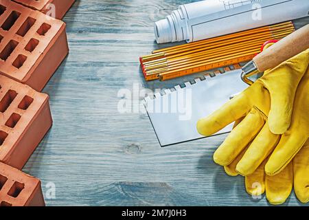 Red bricks safety gloves wooden meter blueprints bricklaying trowel ...