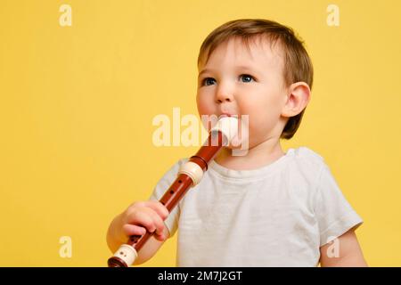 Toddler baby with a flute wind musical instrument on a studio yellow ...