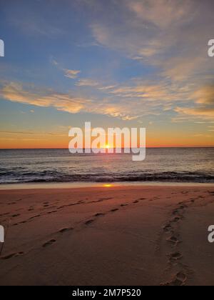A vertical shot of a sandy beach with foamy waves and a sunset view in ...