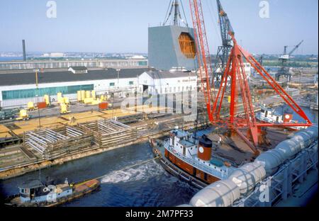 A lift barge/crane, being propelled by a tugboat on each side, carries ...