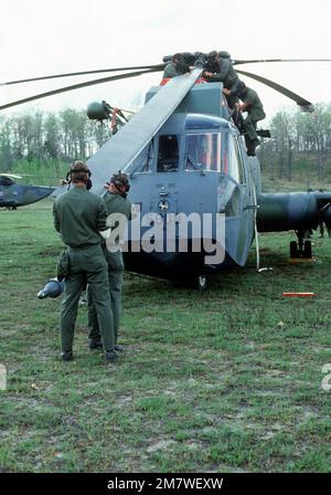 Crew members wearing gas masks, replace a rotor blade on an HH-3E Jolly ...