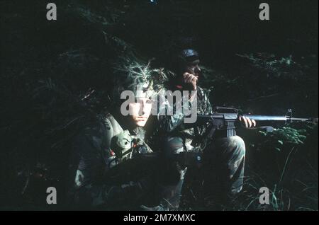Camouflaged security police, armed with M-16 rifles, enter a clearing ...