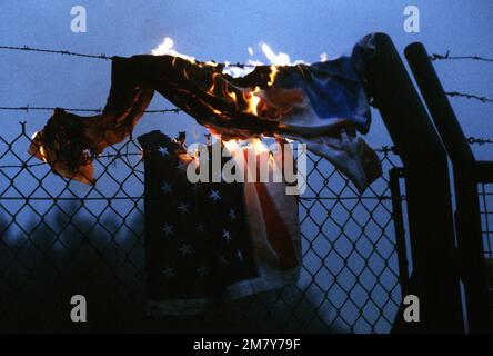 An American flag is burned on the perimeter fence by protesters ...