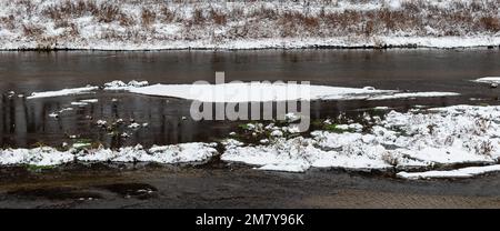 Scenic view of quiet transparent river with spots of white snow on the ...