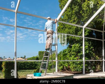 Handyman cleaning outdoor screen pool cage enclosure with power washer ...