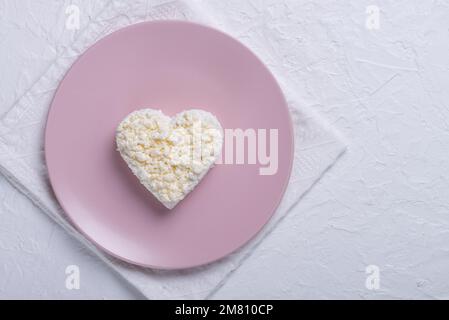 Heart shaped cottage cheese in a plate on a white table. Copy space for ...