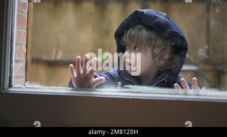 Toddler child leaning on window looking through glass. Baby two year ...