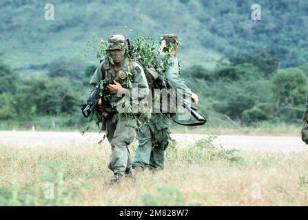 A soldier wearing camouflage, armed with an M16A1 rifle, takes cover in ...
