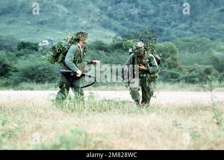 A soldier wearing camouflage, armed with an M16A1 rifle, takes cover in ...