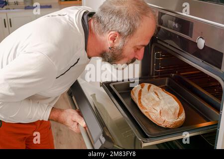 Older man with beard putting bread in the oven of his house Stock Photo ...
