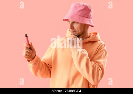 Thoughtful young man in bucket hat with disposable electronic cigarette ...