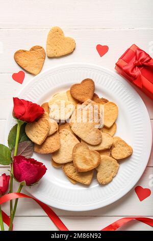 Plate with heart shaped cookie and rose flowers on light background ...