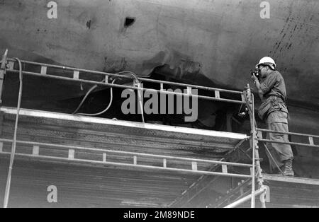 A photographer records the damage to the hull of the guided missile ...