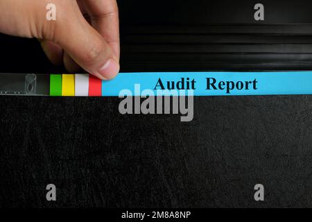 Hand picking audit report file record in black binder folder. Auditing ...