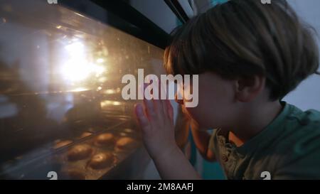 Child staring at oven. Kid looking at cookies baking inside heating ...