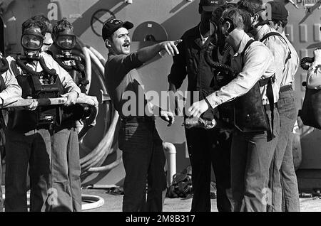 A crewman wearing oxygen breathing apparatus aims the nozzle of a water ...