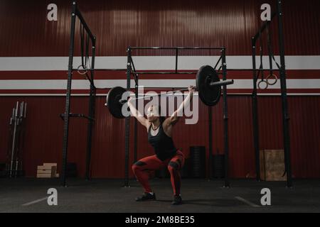 Crossfit athlete doing overhead squat with barbell. Portrait of young ...