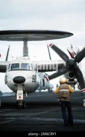 A plane director guides an E-2C Hawkeye aircraft on the flight deck of ...