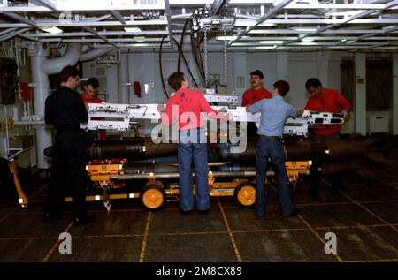 Weapons technicians lower a BDU-45/B 500-pound practice bomb onto an ...